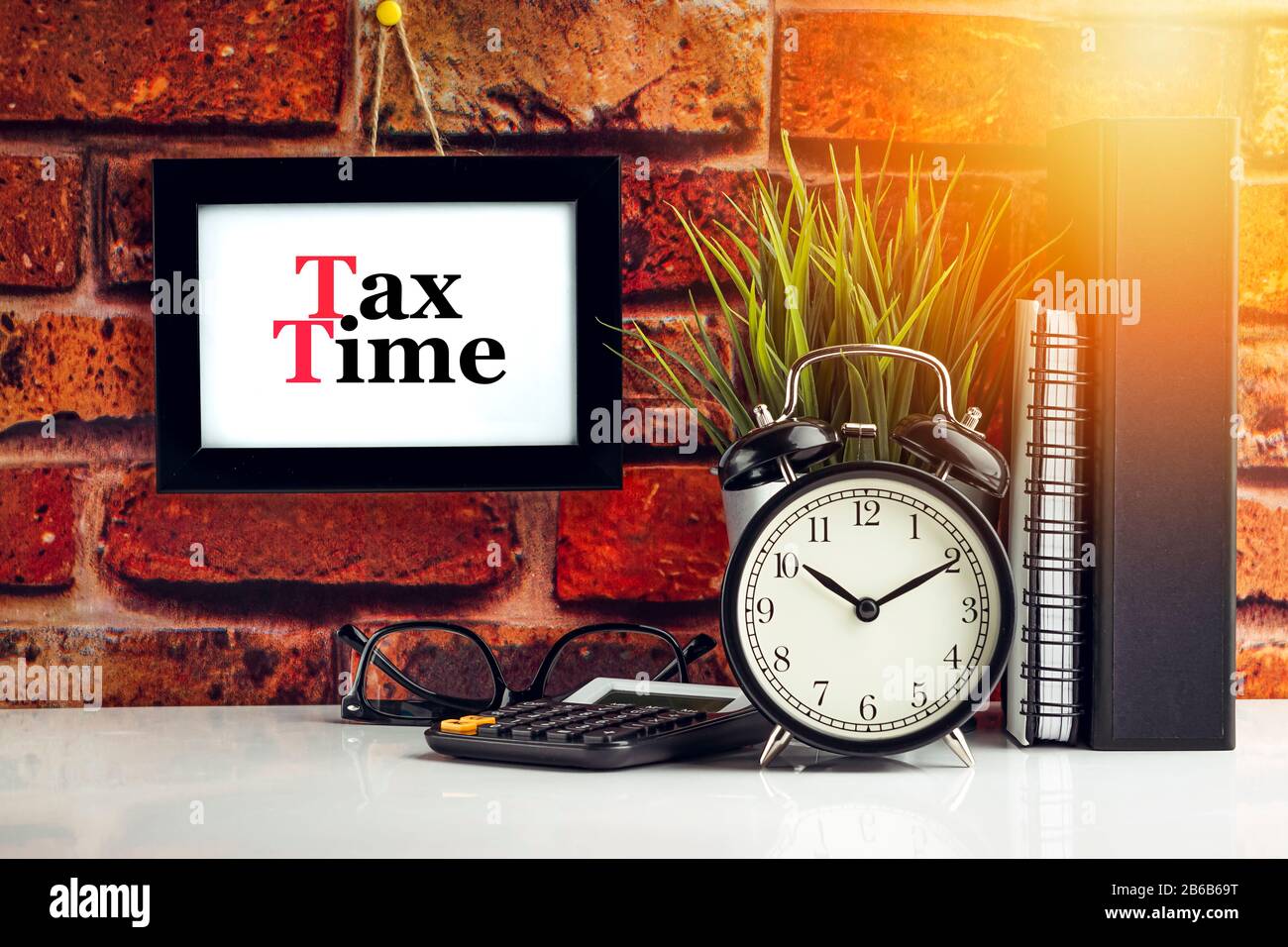TAX TIME text with alarm clock, books and vase on brick background ...