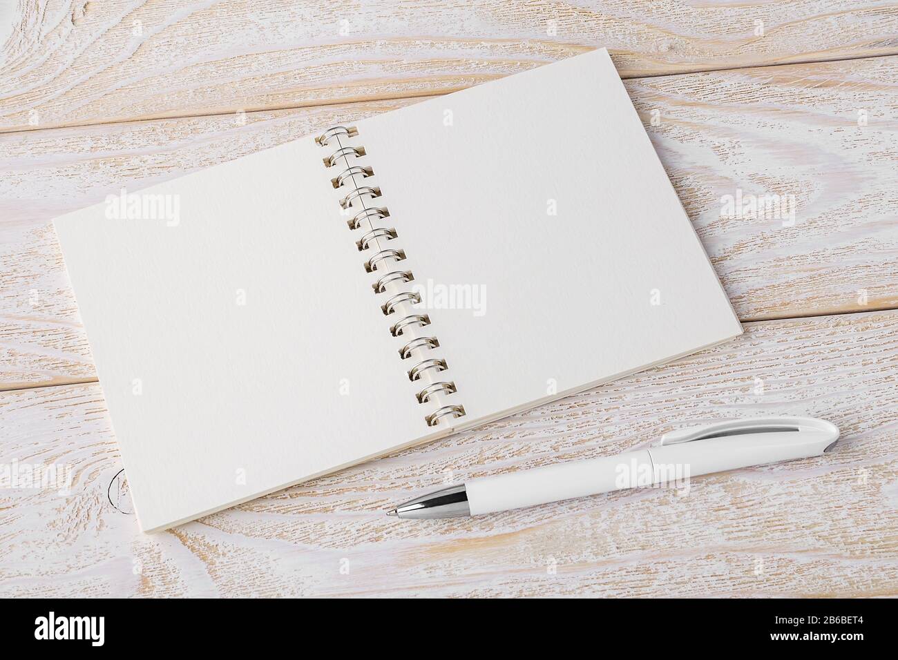 Opened spring notepad and white ballpoint pen on a white wooden ...