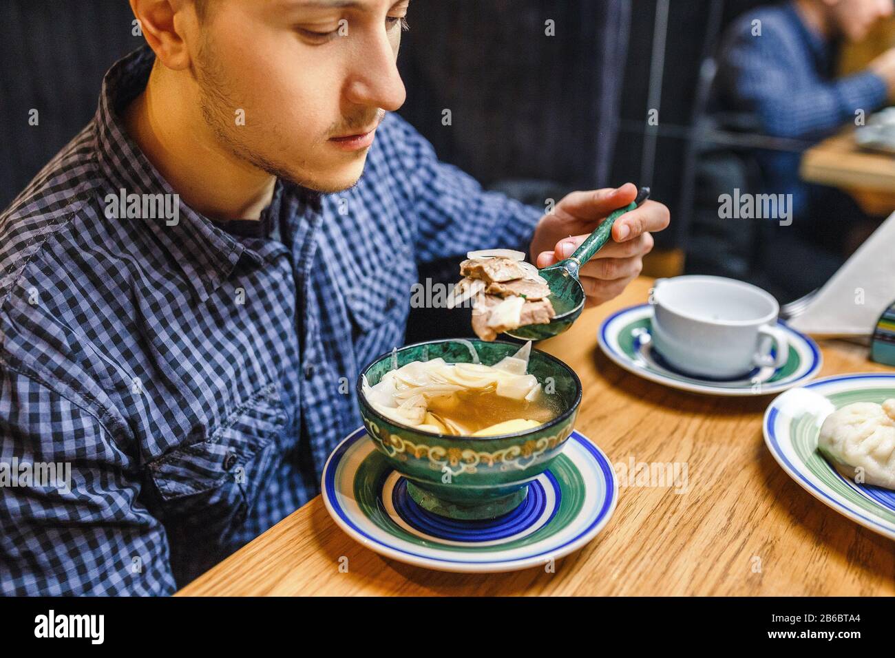 Man eating traditional asian soup from patterned wooden plate Stock ...