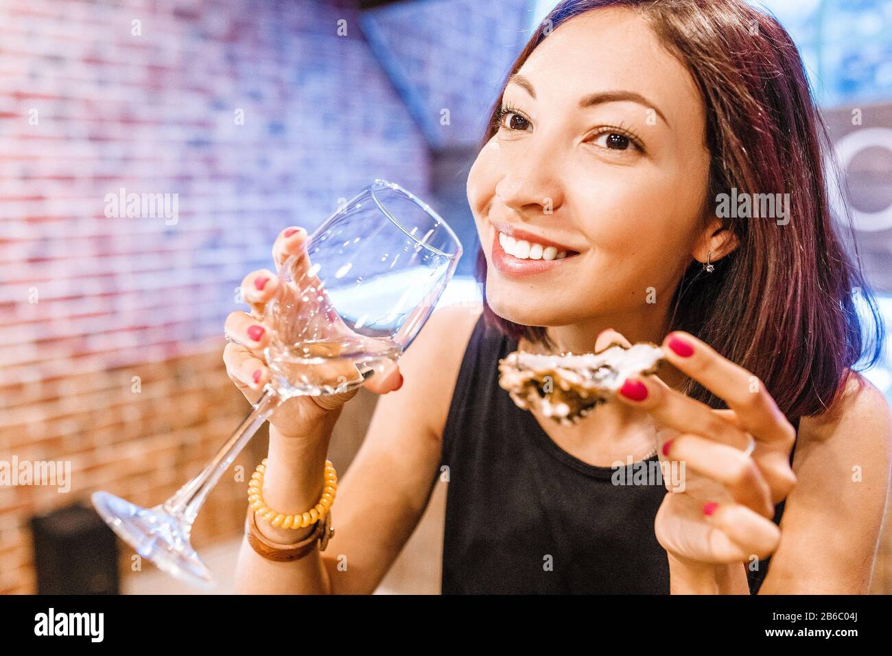 Young woman eating oyster shellfish and drinking white wine in a luxury ...