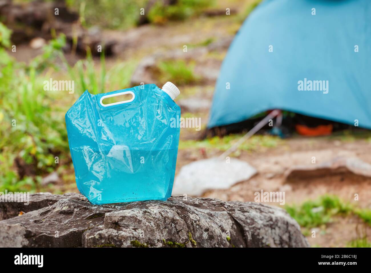 A large bottle or a water tank on a camping background with a tent in ...