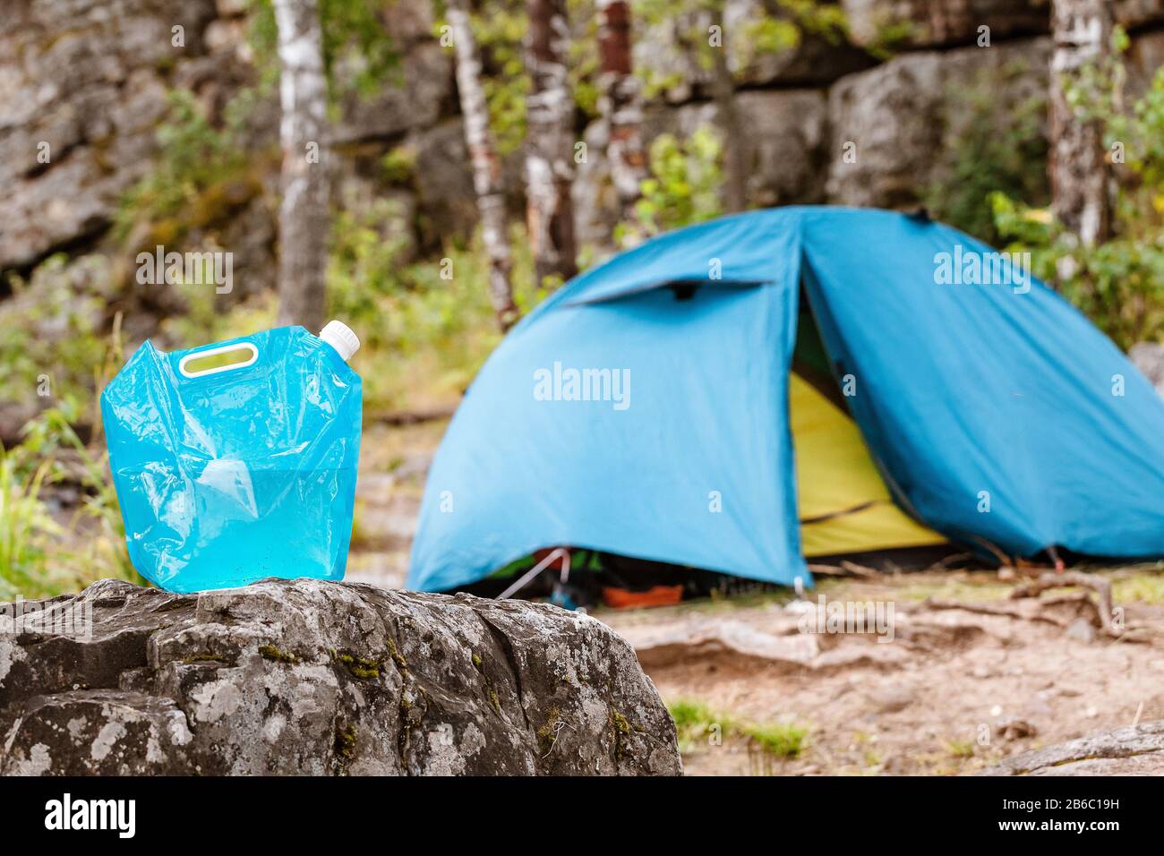 A large bottle or a water tank on a camping background with a tent in ...