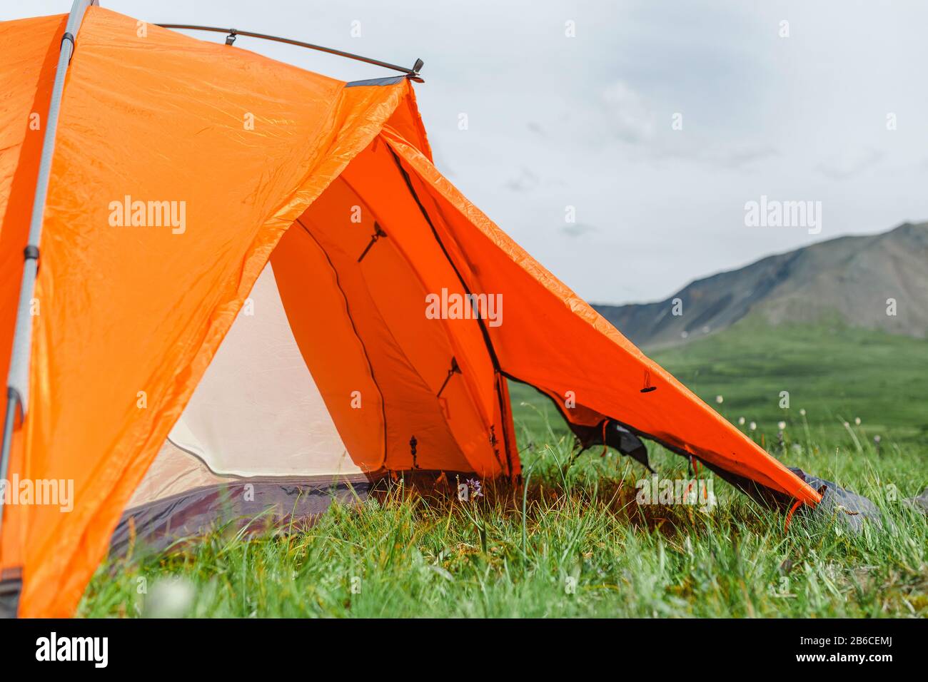 A bright orange tent is set on a beautiful lawn in the mountains, the ...