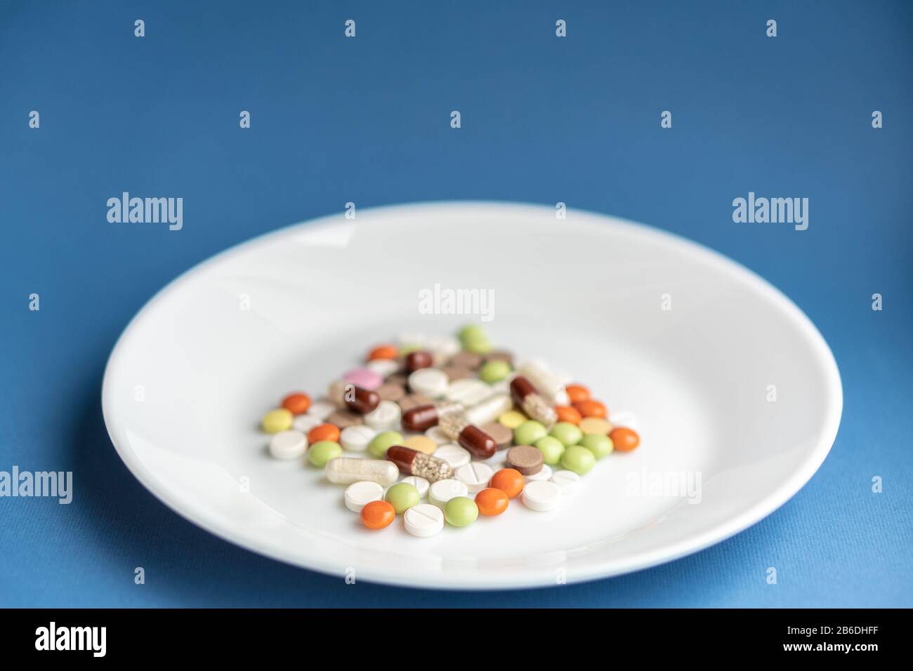 Pills on a white plate. Multi-colored pile of pills on a classic blue ...