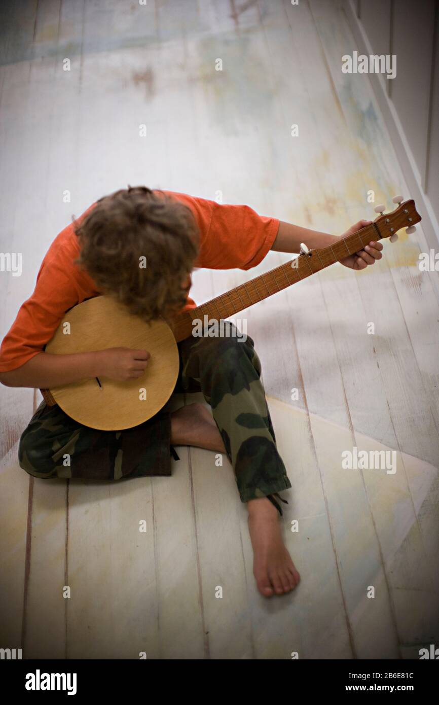 Young boy sitting on the floor playing a banjo Stock Photo - Alamy