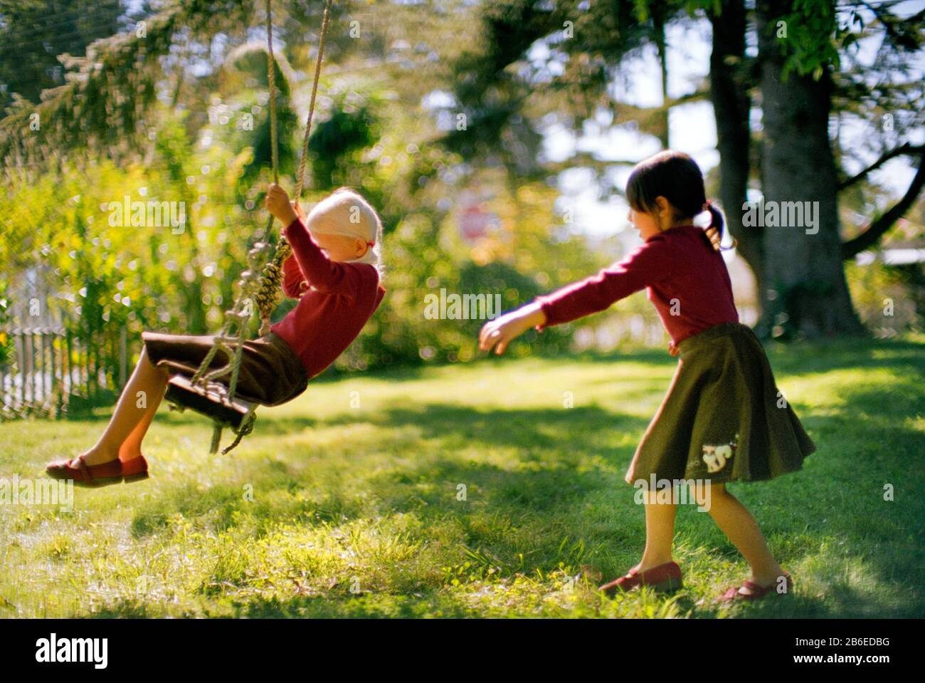 Little girl pushing her friend on tree swing Stock Photo - Alamy