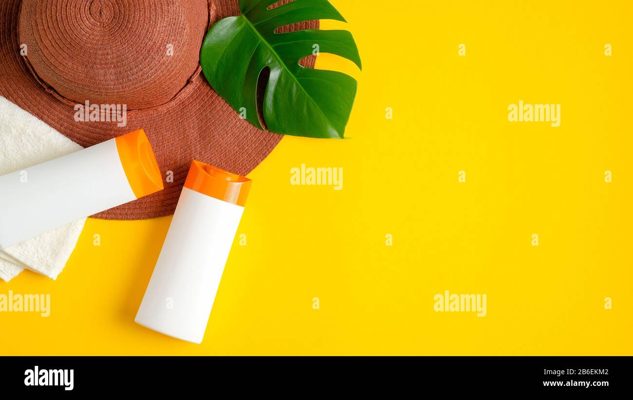 Flat lay sunscreen cream bottles, female beach hat and tropical leaves ...