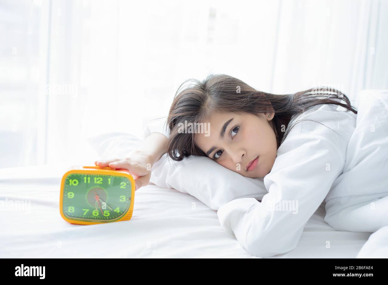 Asian woman happy waking up and turning off the alarm clock having a ...