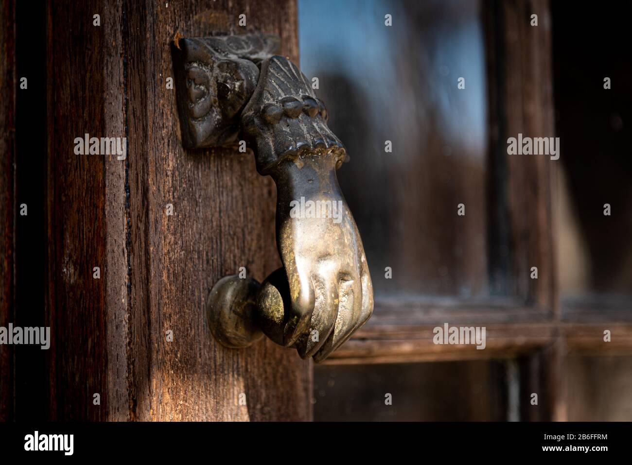 Old rusty and grungy hand shaped golden door knocker on a wooden door ...