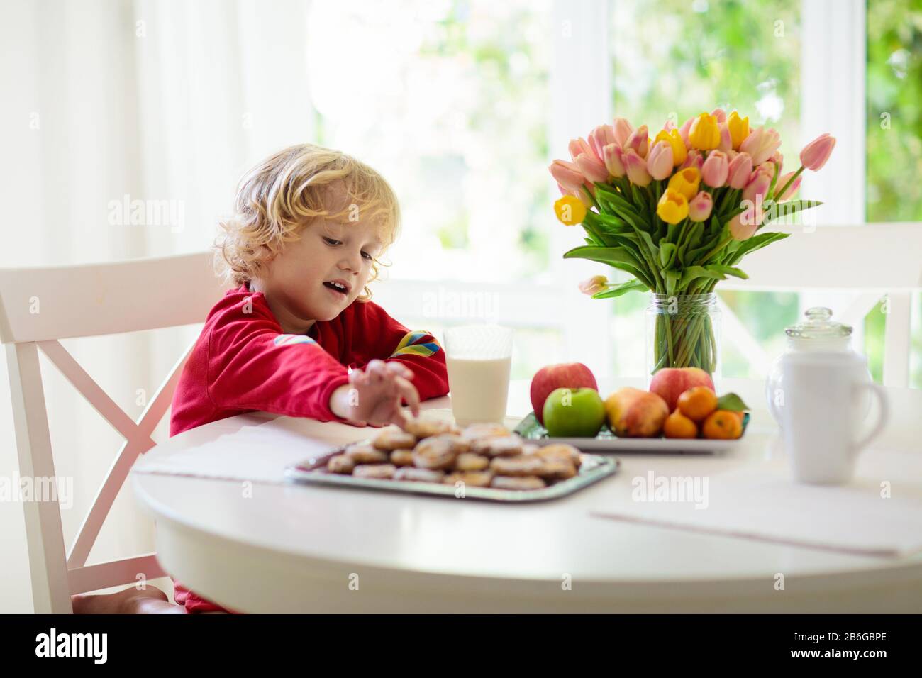 Child eating breakfast. Kid drinking milk with fresh homemade cookies ...