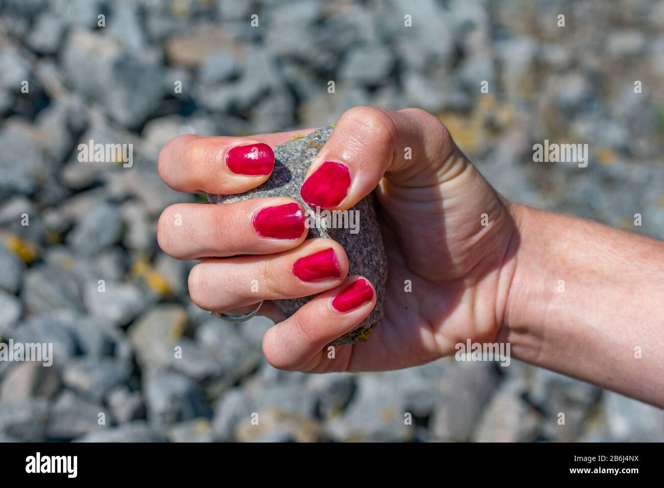 Female hand with red nails holding stone Stock Photo - Alamy