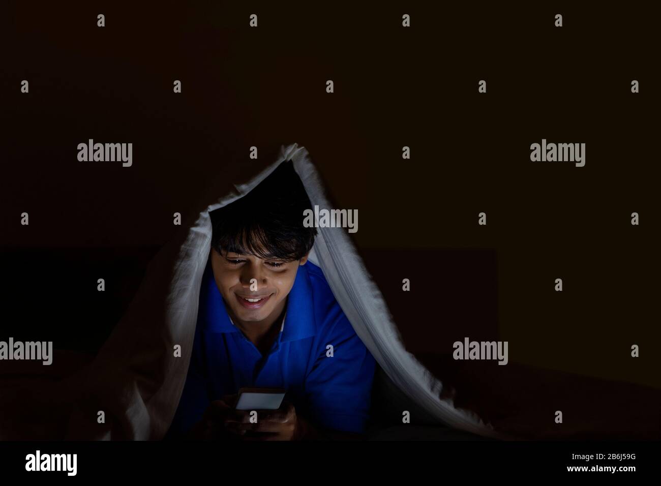 Teenage boy texting on his mobile phone under a blanket Stock Photo - Alamy