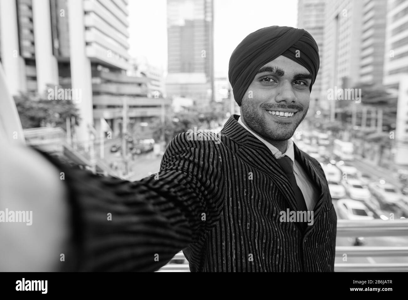 Happy young handsome Indian Sikh businessman wearing turban in the city ...