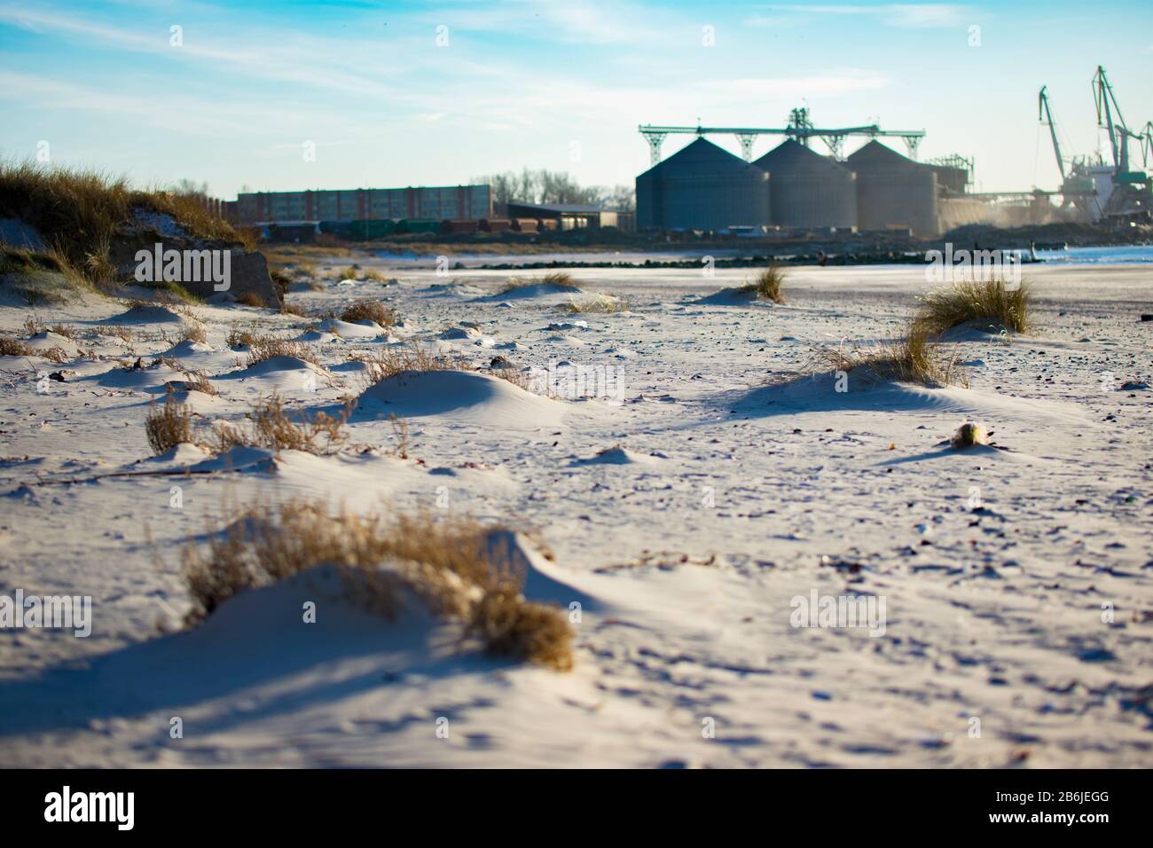 Beach with industrial seaport in background. Silos and cranes (Port of ...