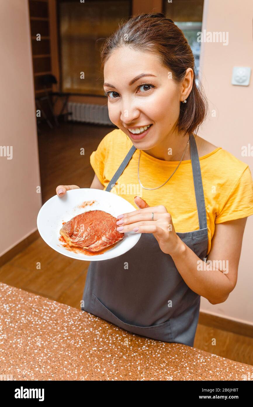 Woman chef in apron with Fresh beef steak on a kitchen table with ...