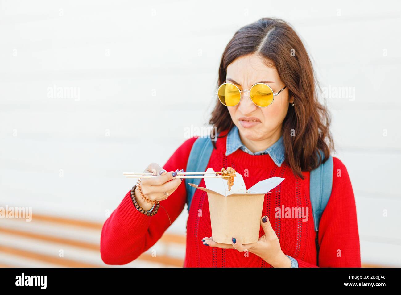 Girl with an expression of displeasure eating Asian street food wok ...