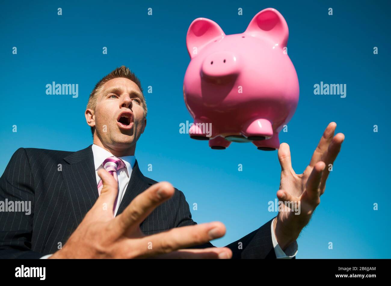Nervous businessman reaching out to catch a piggy bank falling from the ...