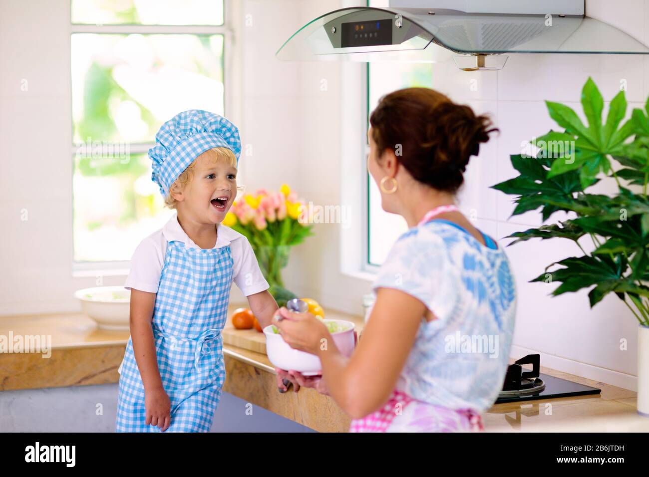 Mother and kid cook in white kitchen. Mom and child cooking at home ...