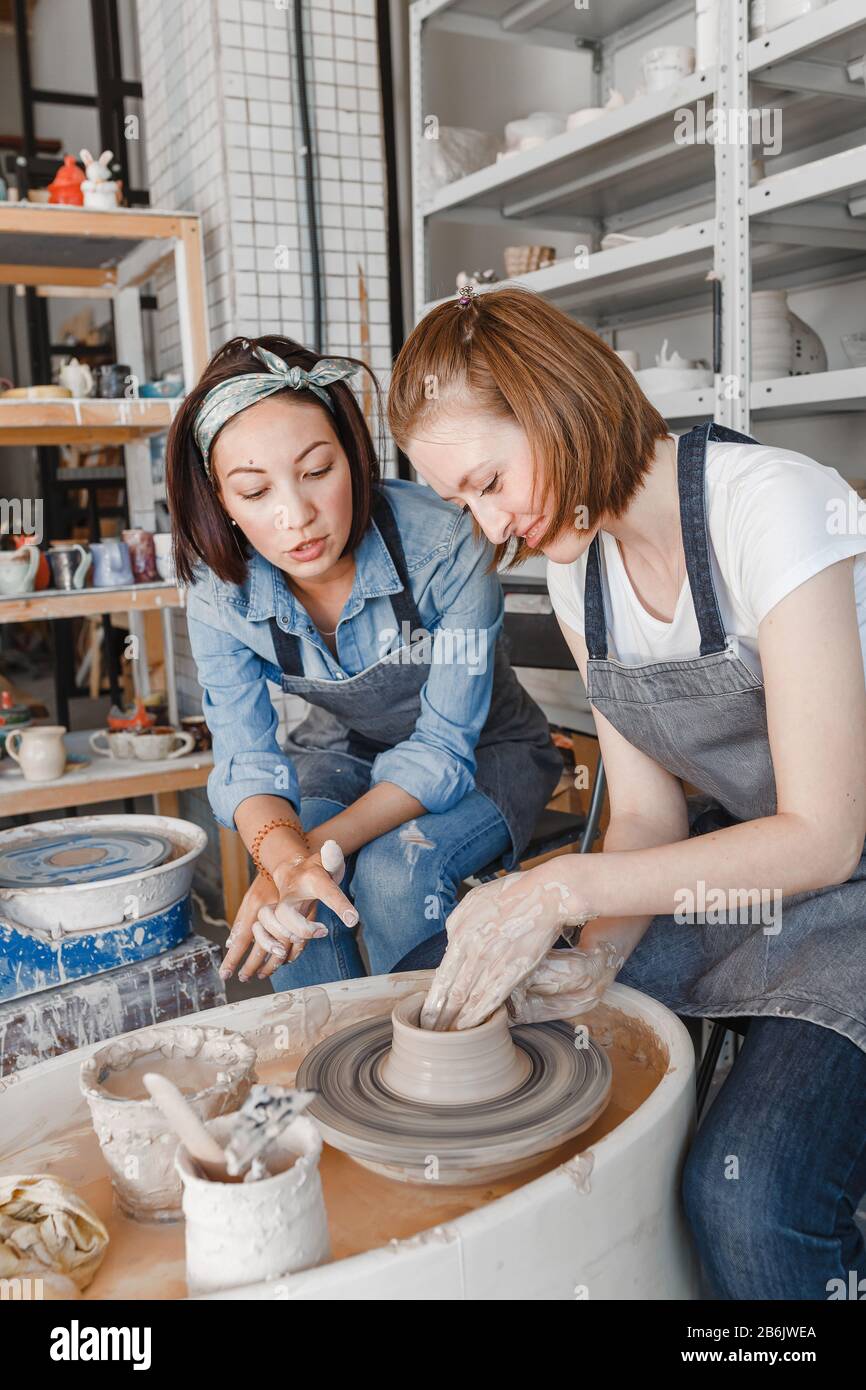 Two girls friends smiling and talking while working on potters wheel ...