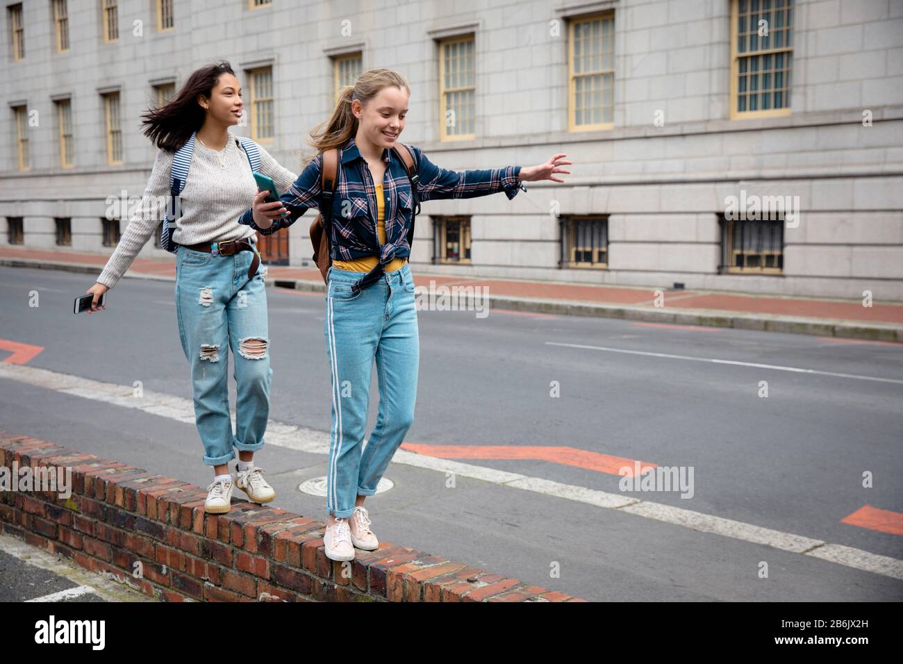 Side view of friends walking on a low wall Stock Photo - Alamy