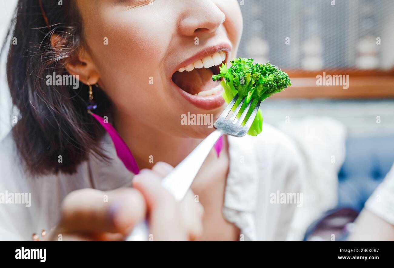 Portrait of happy smiling young casual woman eating broccoli in ...