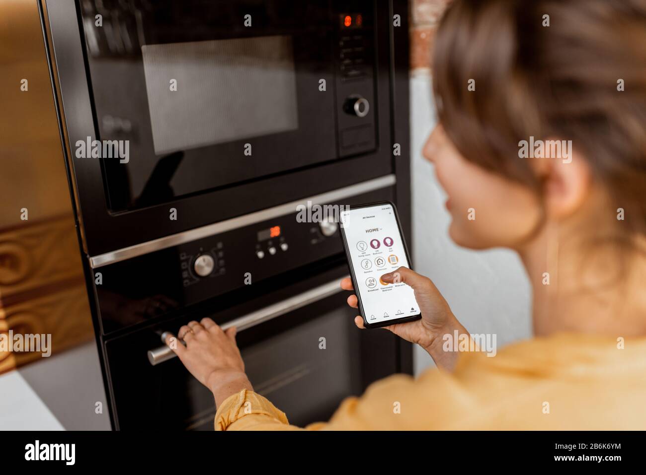 Woman controlling smart kitchen appliance using mobile phone at home ...