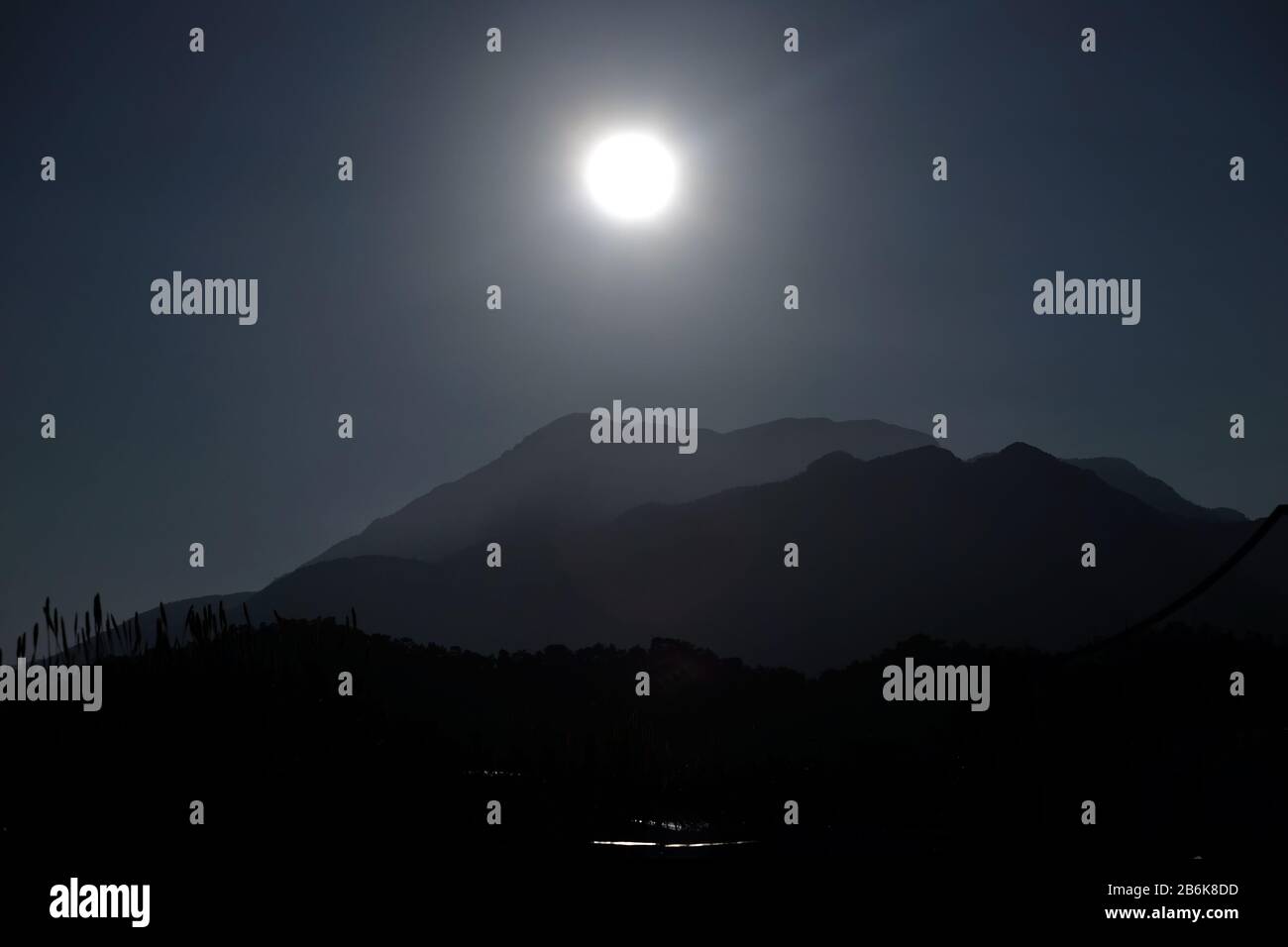 Sunset with round sun above high mountain silhouettes in back light ...