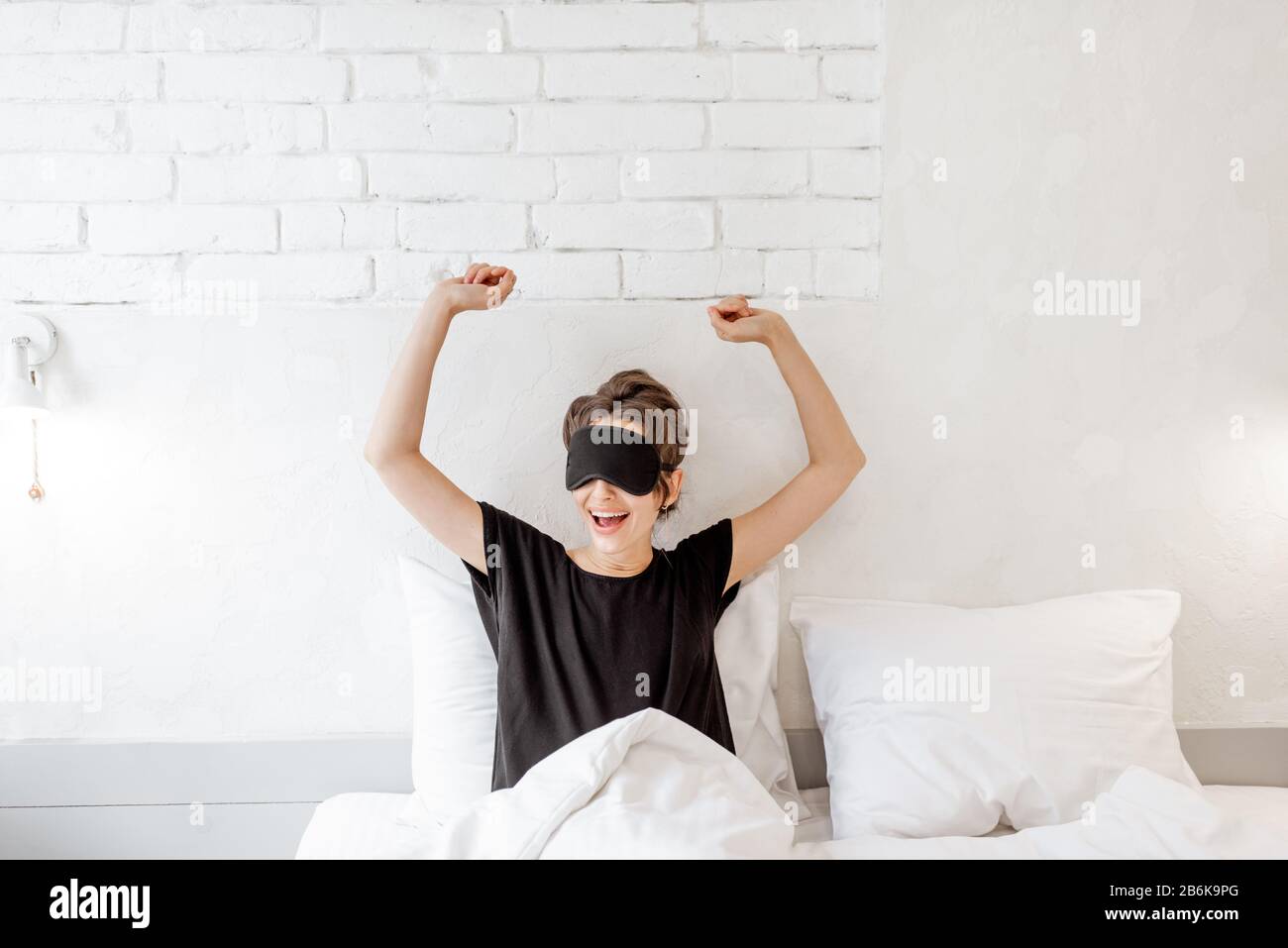 Young woman in sleeping mask waking up in the bedroom. Good morning ...