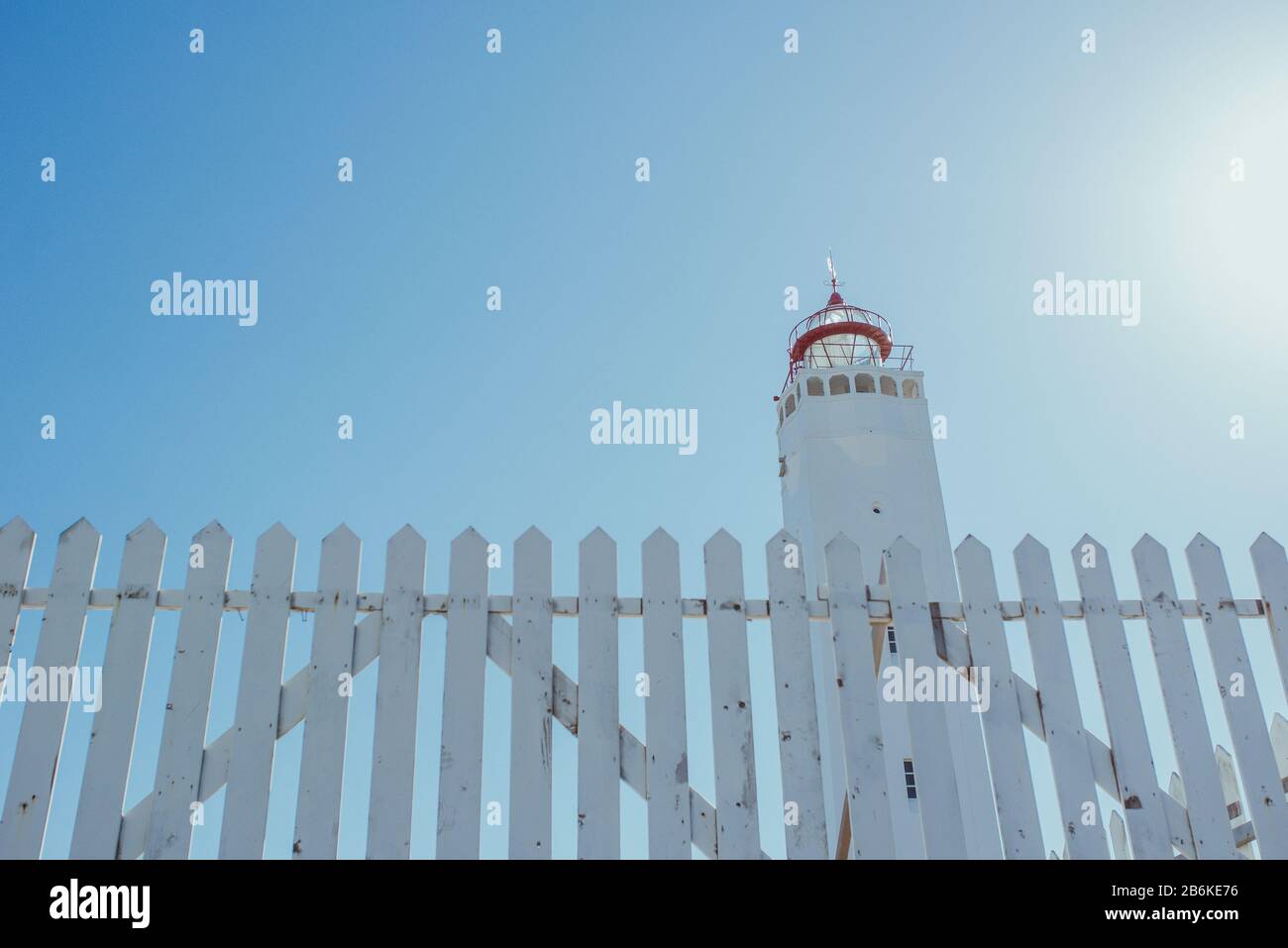 white lighthouse with white fence on blue sky background near the sea ...