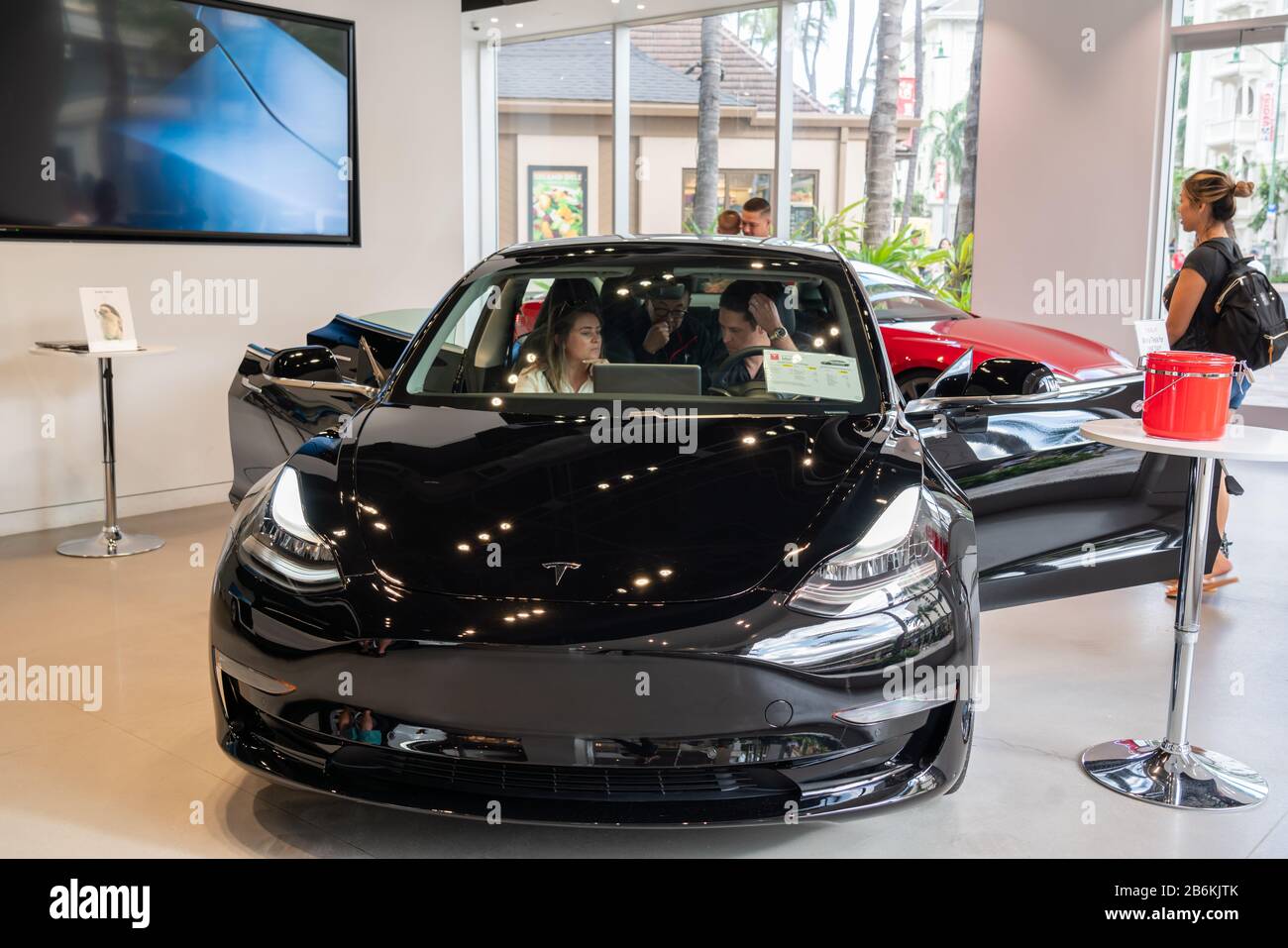 Customers admire a Tesla Model 3 electric vehicle at a Tesla store ...