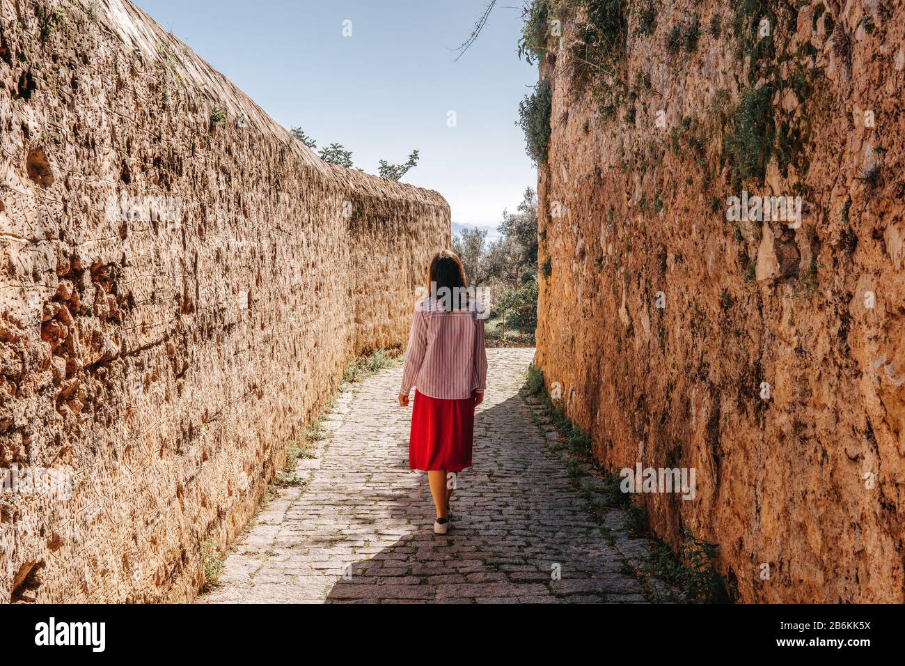 Young woman is walking between historical walls on a narrow alleyway ...