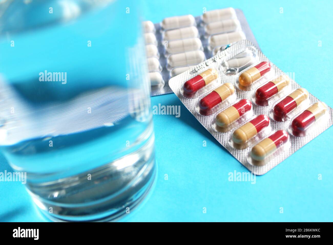 White pills with glass of clear water over blue background, top view ...