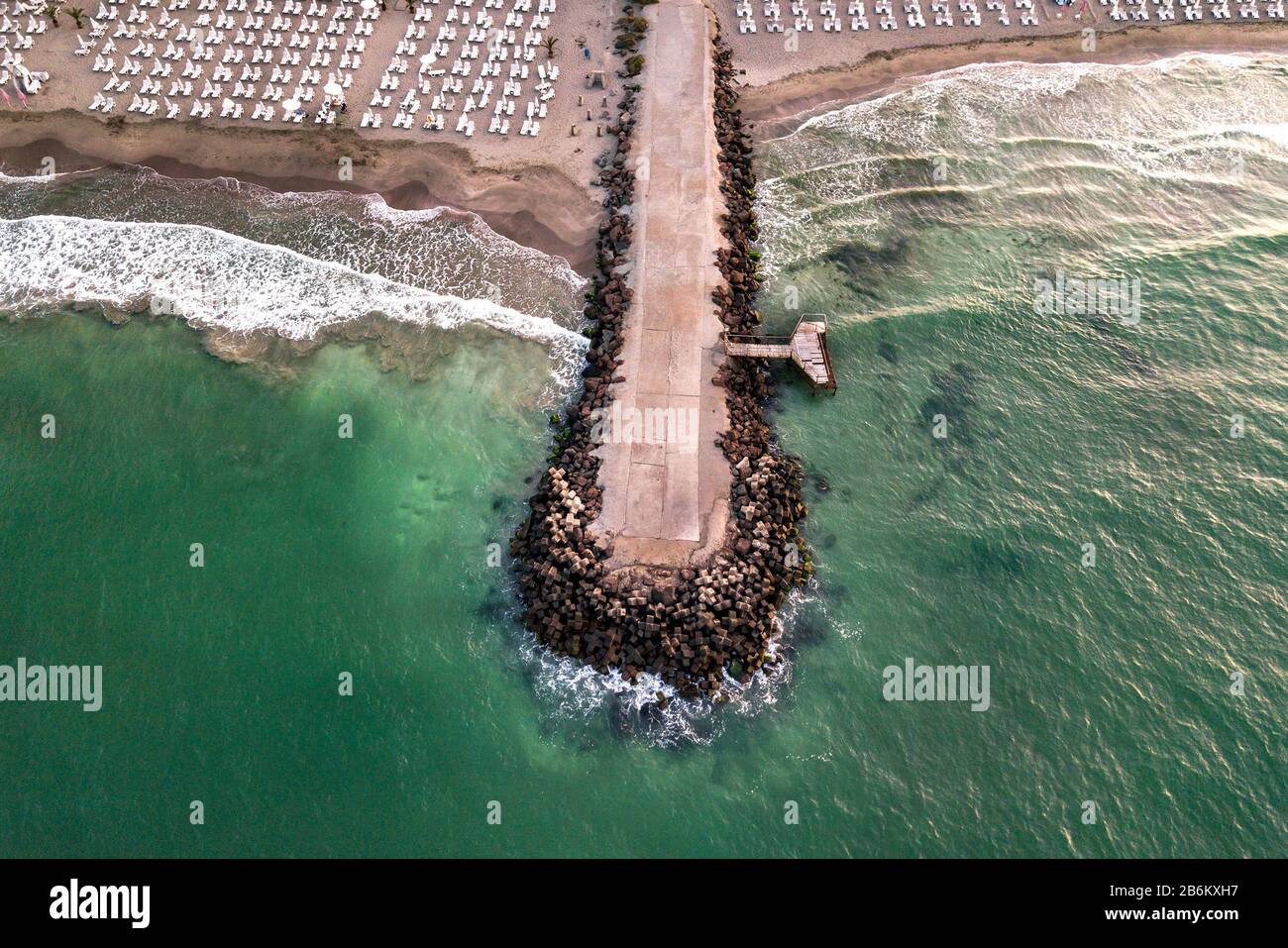Aerial view of a concrete pier on sea shore with wave breaking stones ...
