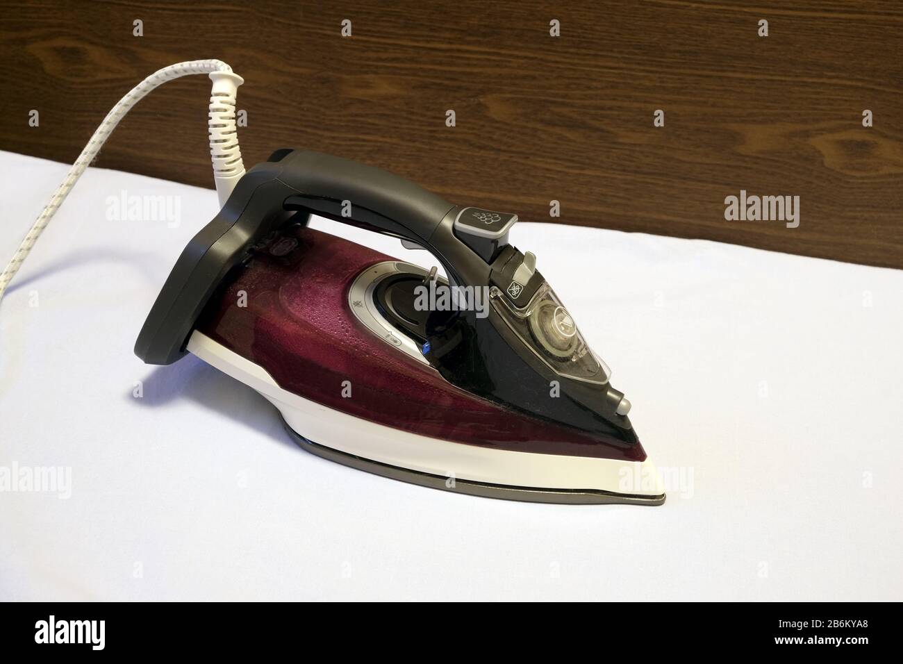 Modern electric iron lays on white fabric surface on the table before ...