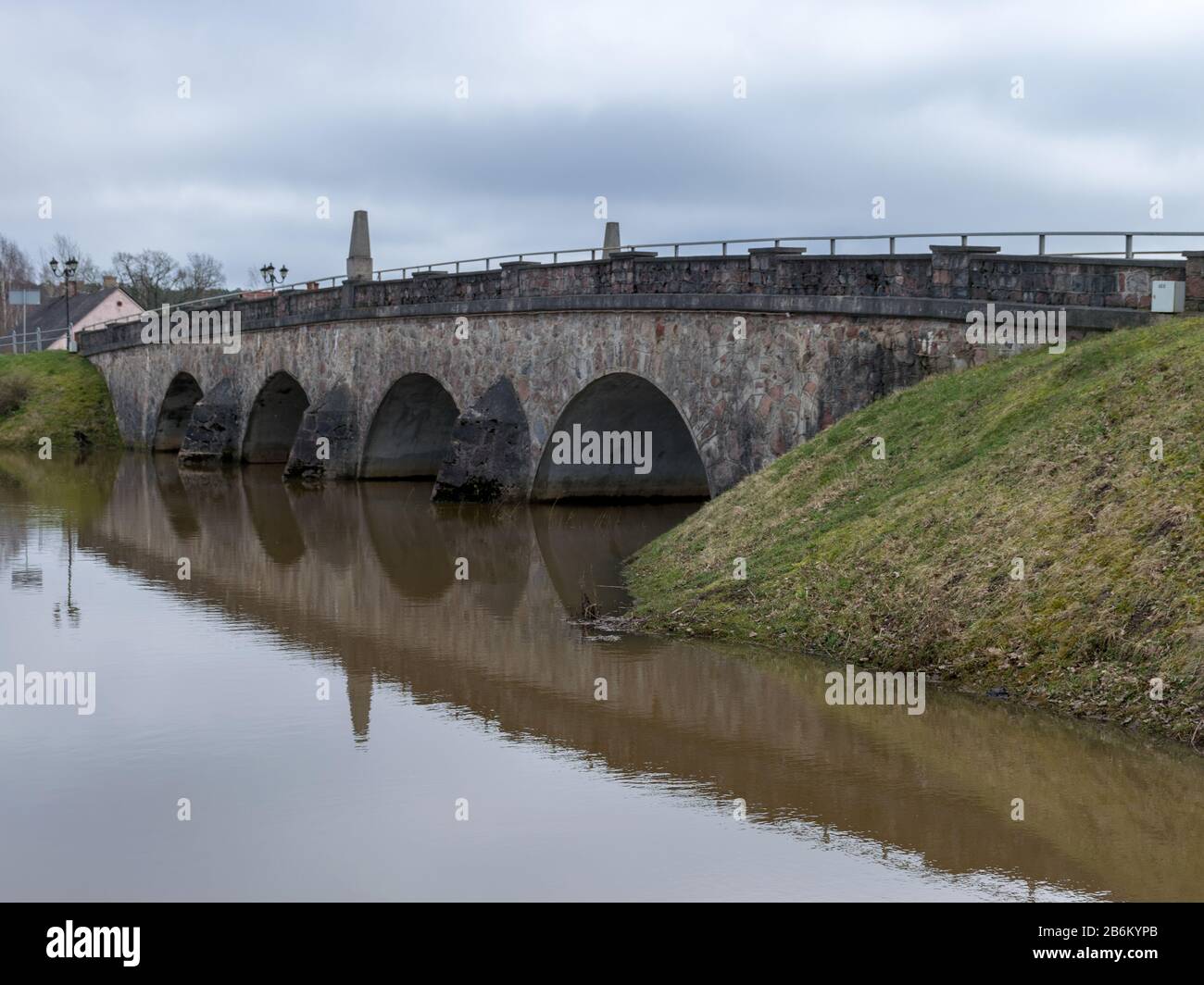 landscape with overflowing river in spring, arched stone bridge over ...