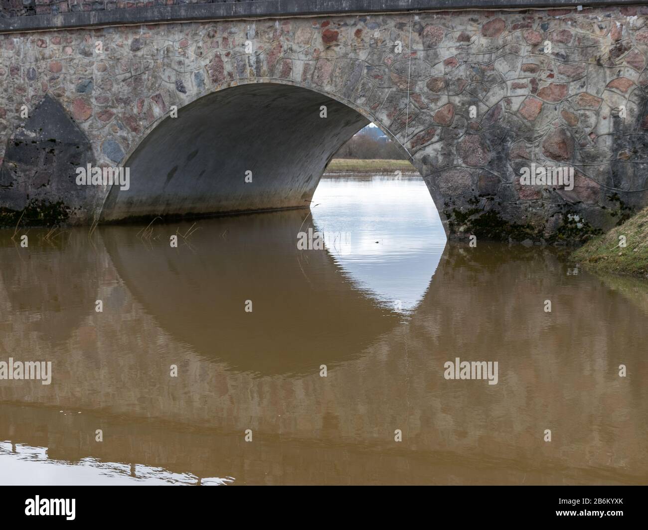 landscape with overflowing river in spring, arched stone bridge over ...