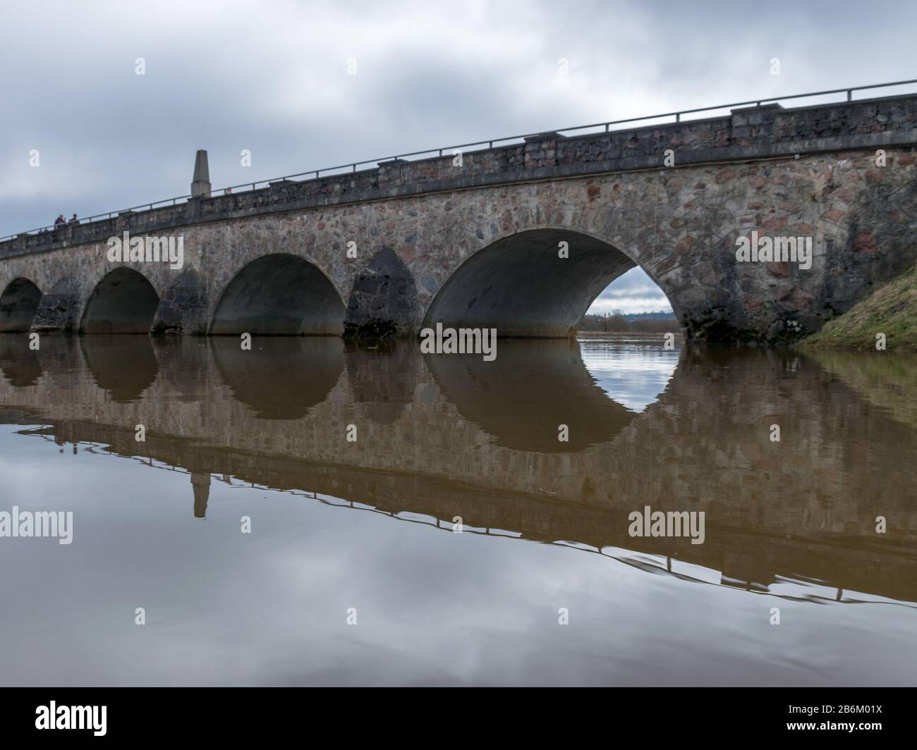 landscape with overflowing river in spring, arched stone bridge over ...