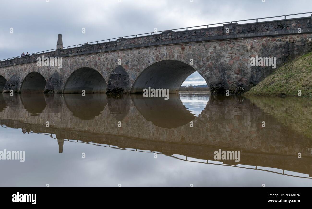 landscape with overflowing river in spring, arched stone bridge over ...