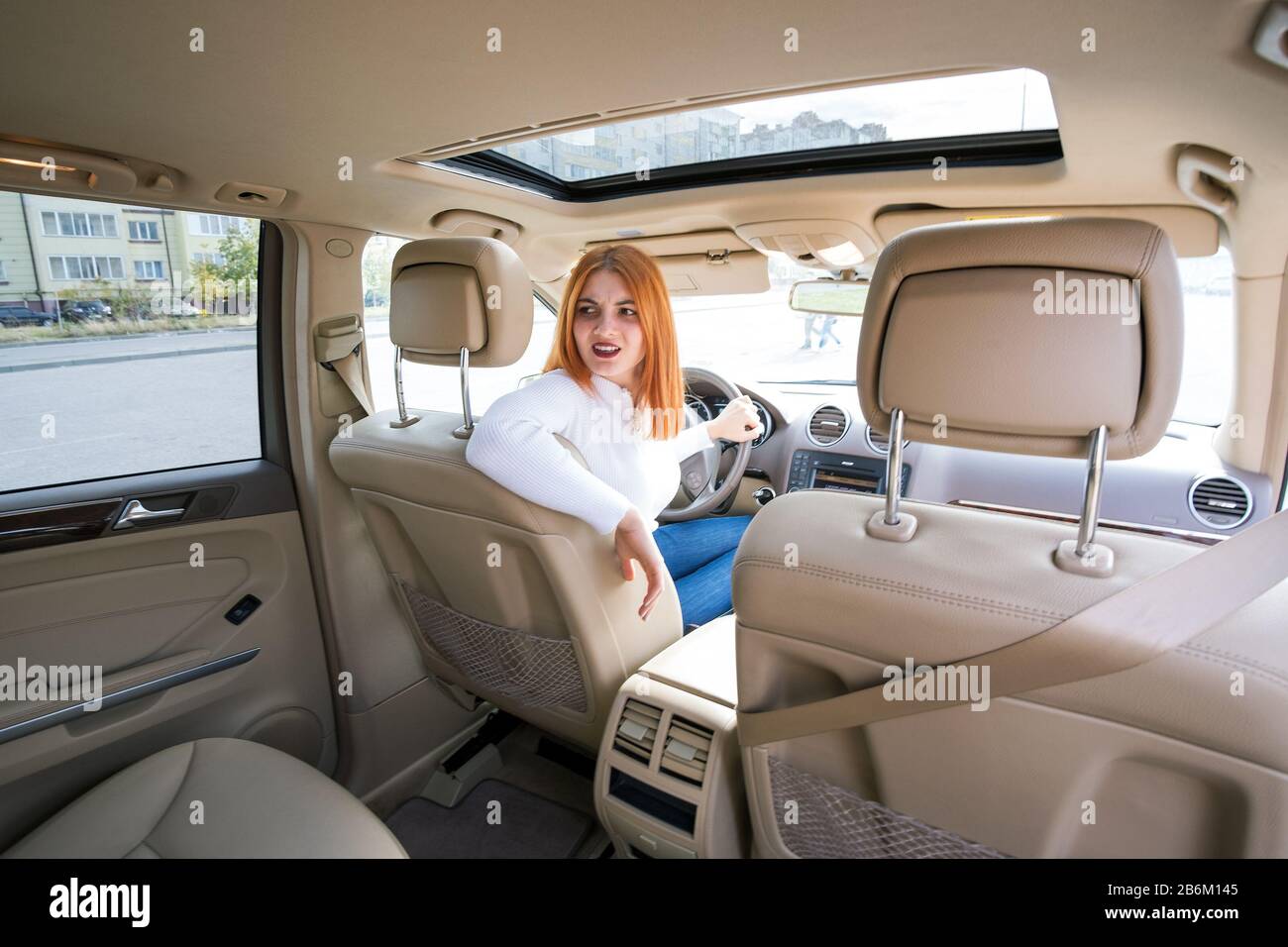Wide angle view of young redhead woman driver driving a car backwards ...