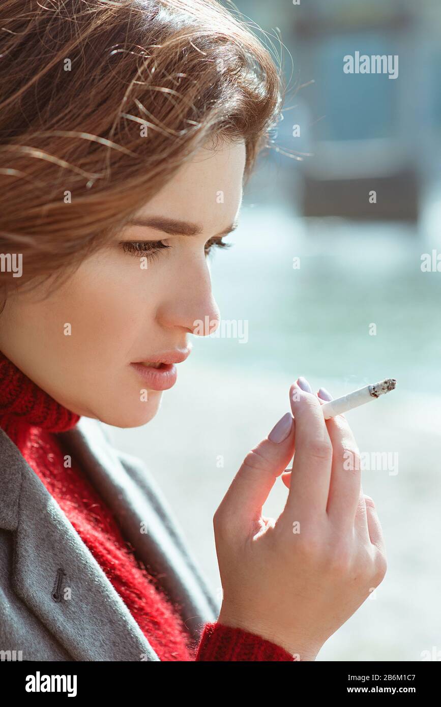 beautiful stylish sad stressful young woman in sweater and coat smoking ...