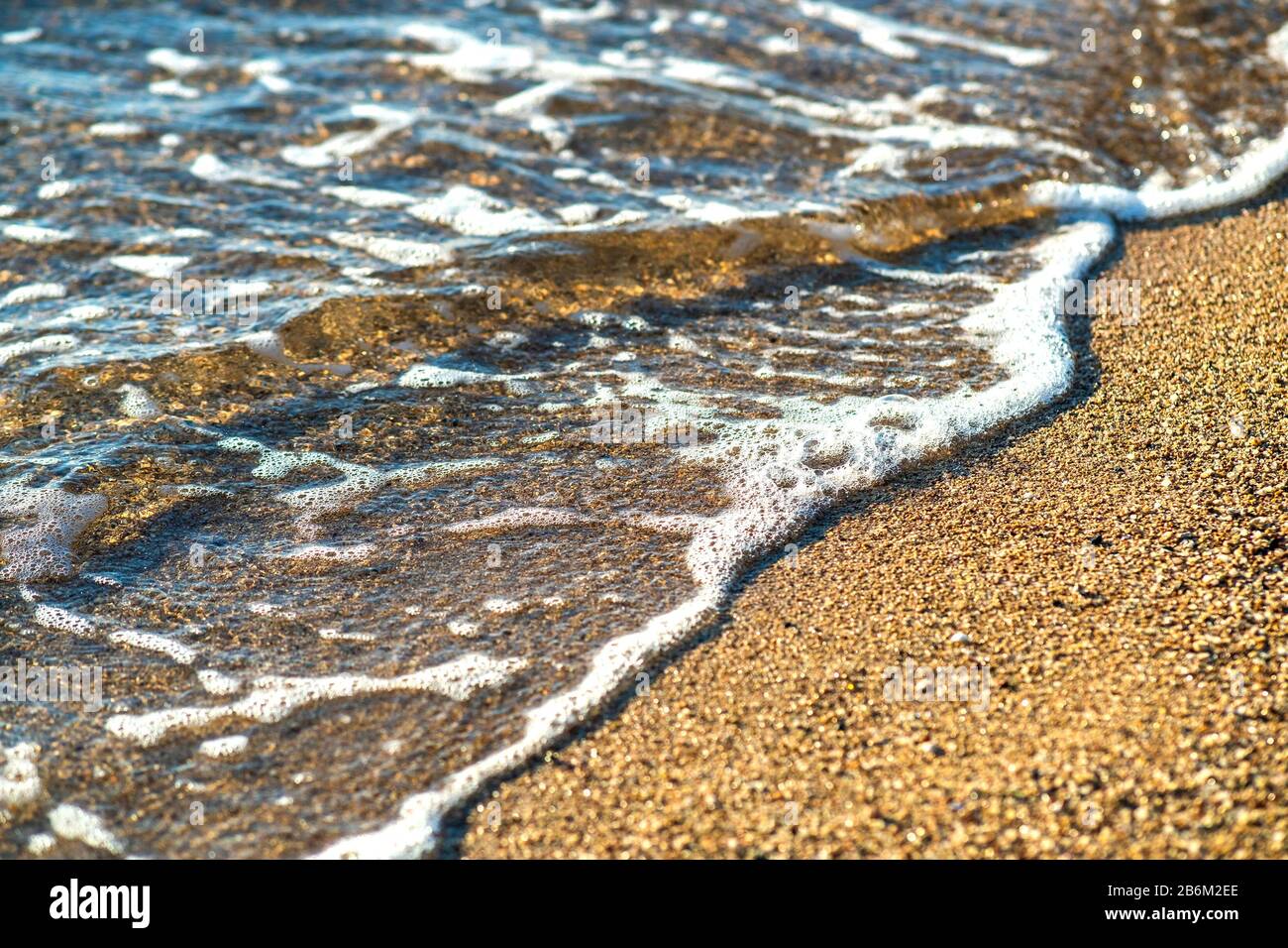 Close up of small sea waves with clear blue water over yellow sand ...