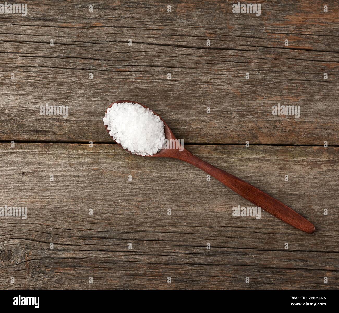 white coarse salt in a wooden spoon, gray table from old boards, top ...