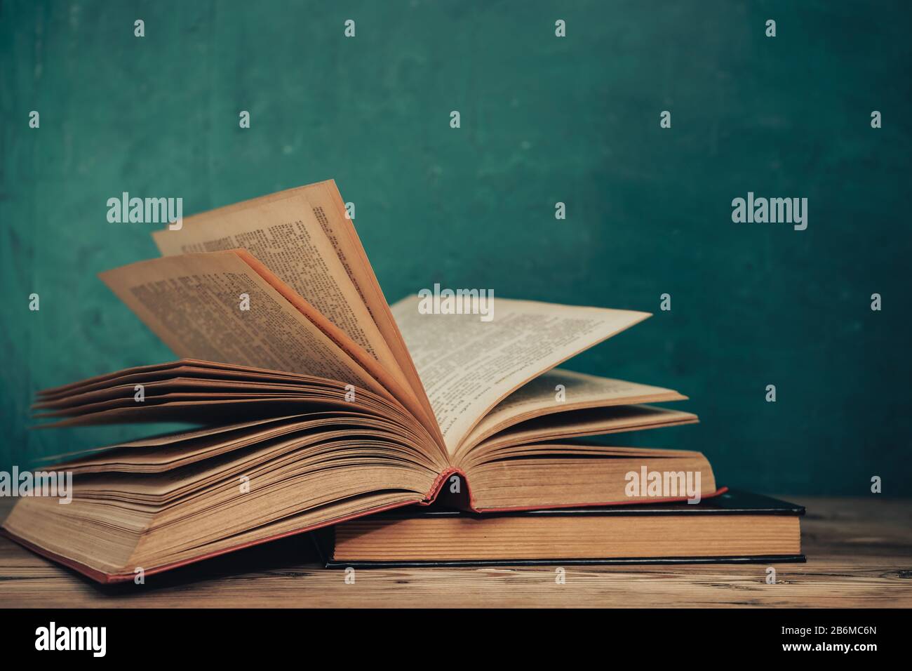 Old open book on a old wooden table and Green wall background behind ...
