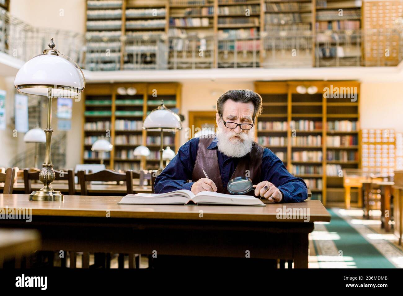 Senior man working in old library, sitting at the table with books and ...