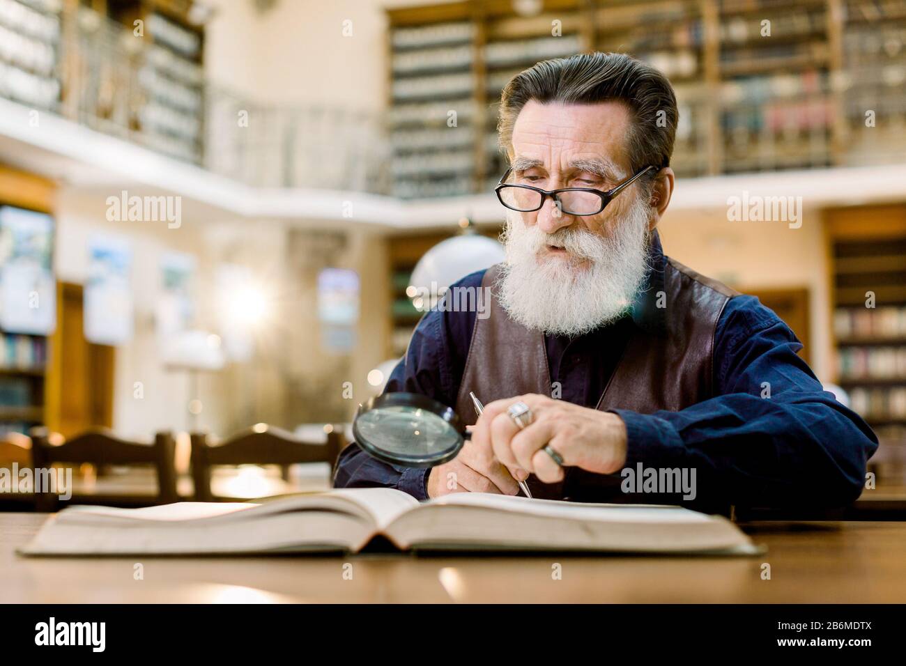 Old man with gray beard, in glasses, vintage clothes, reading a book in ...