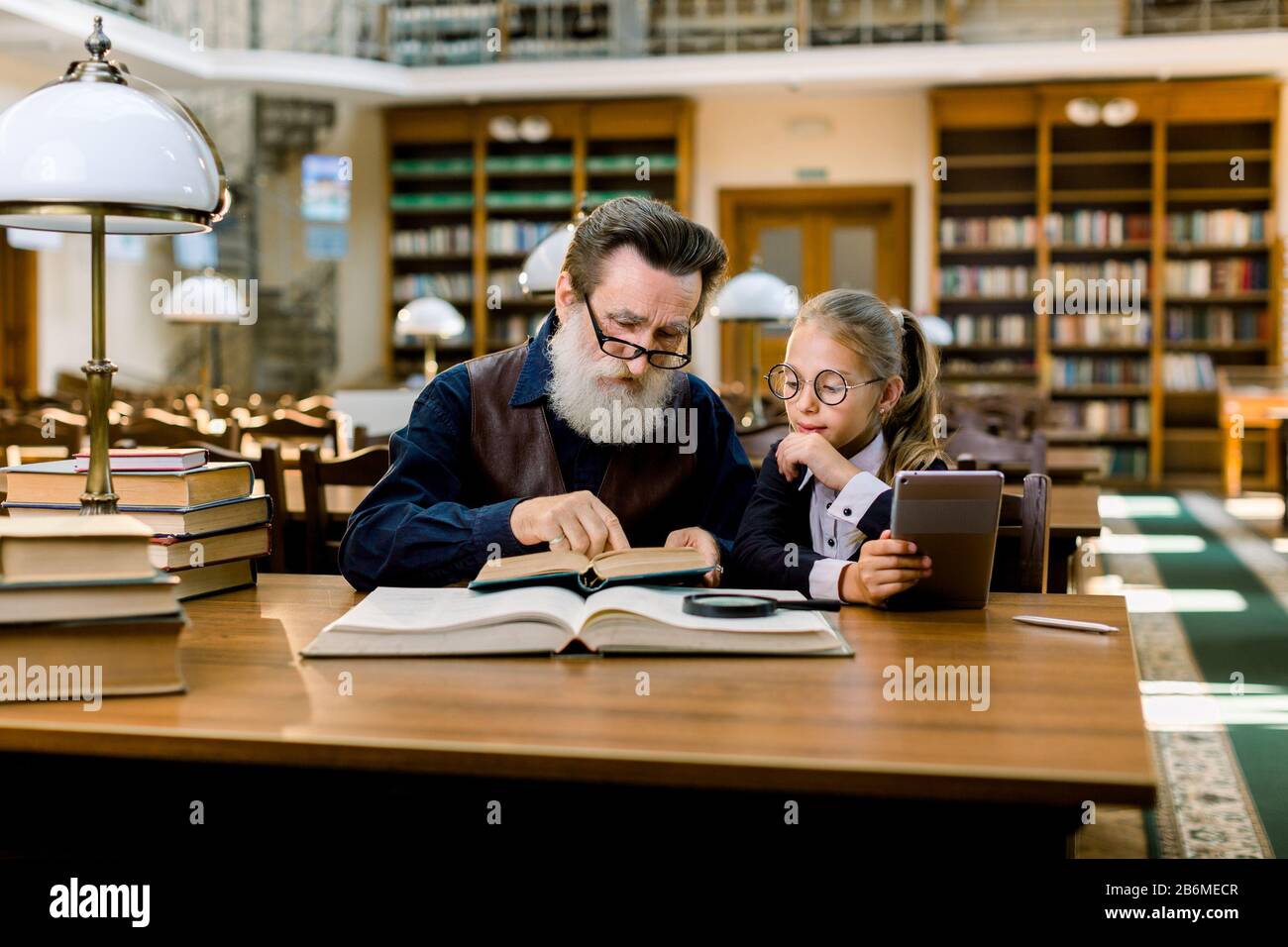 Senior man teacher professor teaching little girl, showing her a book ...