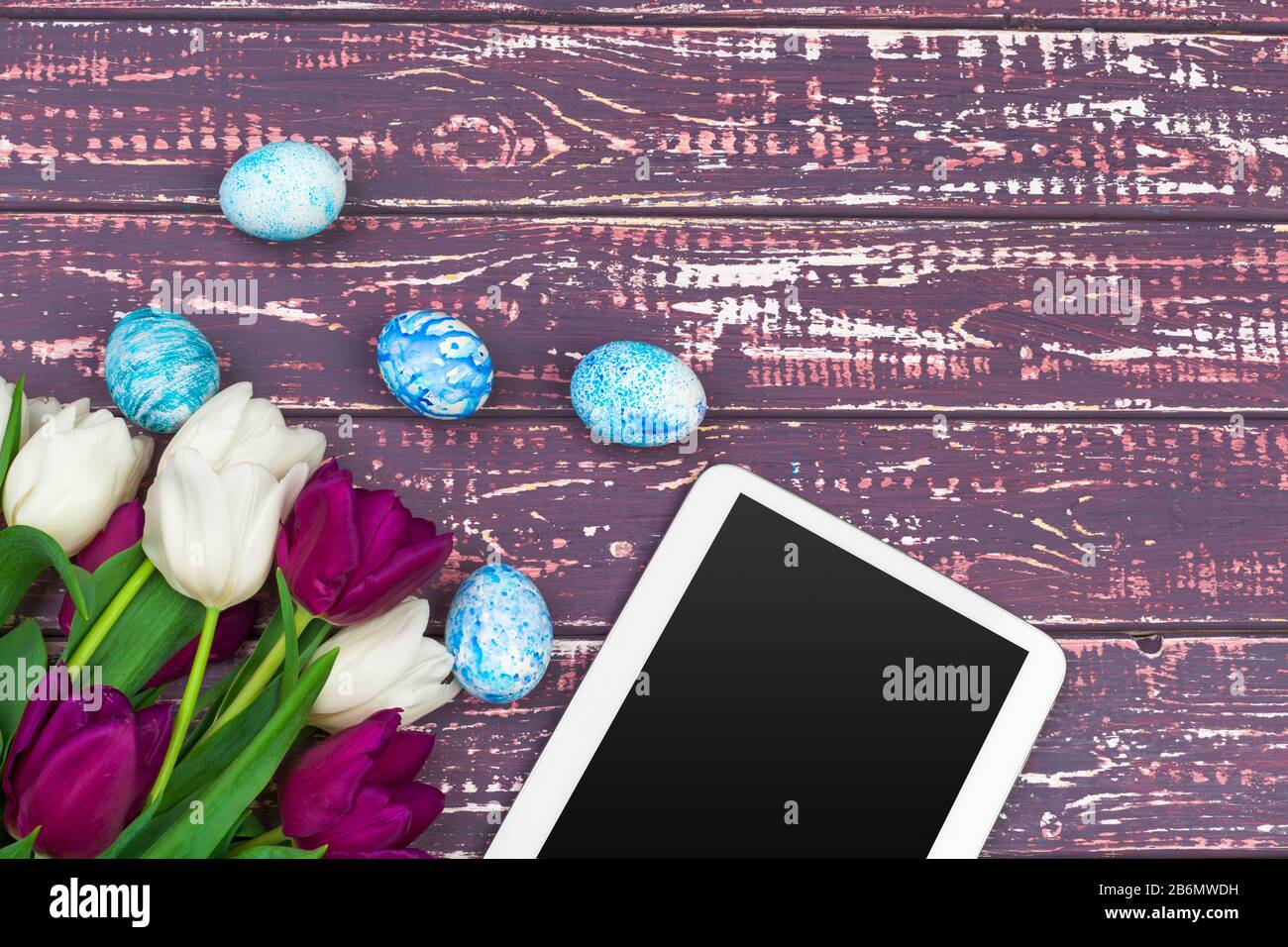 tablet screen for message and colorful tulips and easter eggs on wooden ...