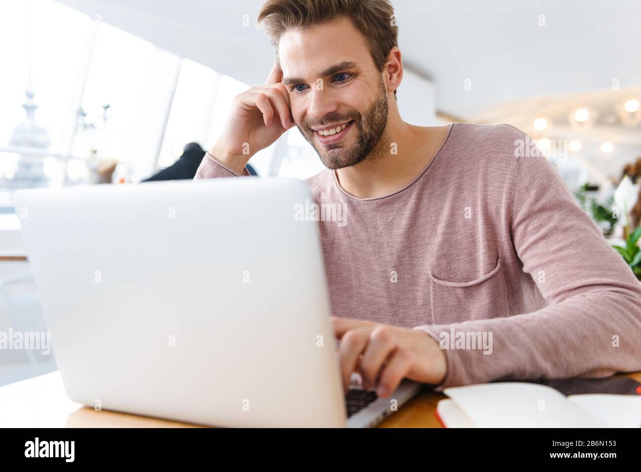 Image of young bearded man working on laptop computer while sitting in ...