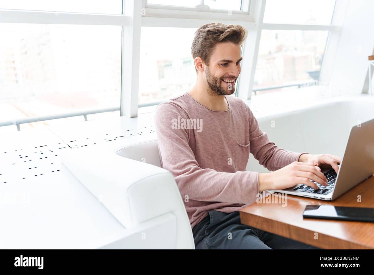 Image of young bearded man working on laptop computer while sitting in ...