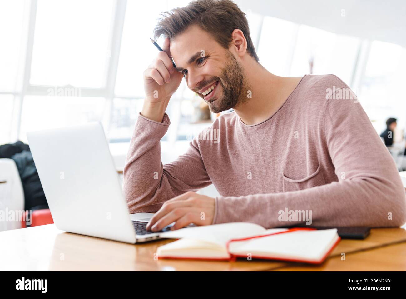 Image of young bearded man working on laptop computer while sitting in ...